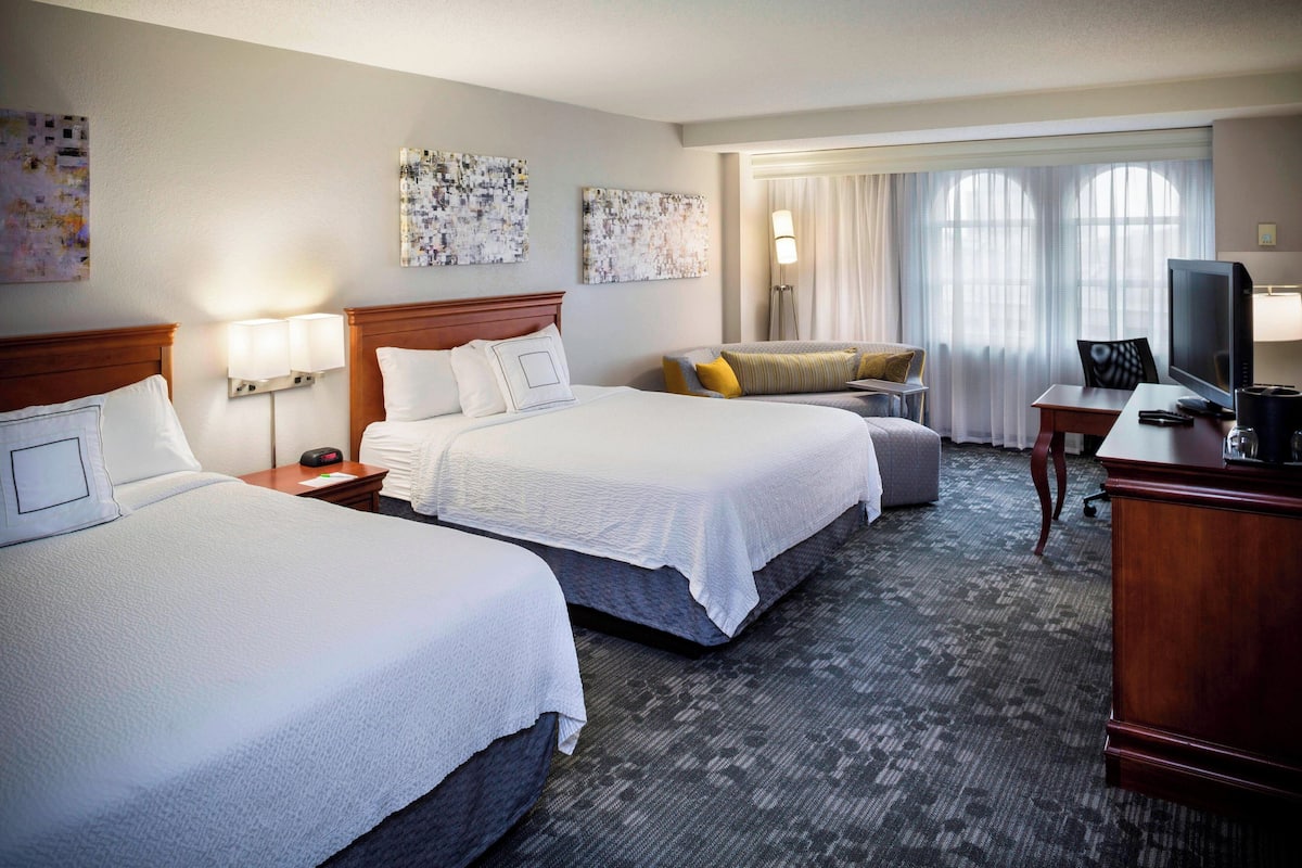 Quarto de hotel com duas camas, uma mesa, uma cadeira e uma televisão.