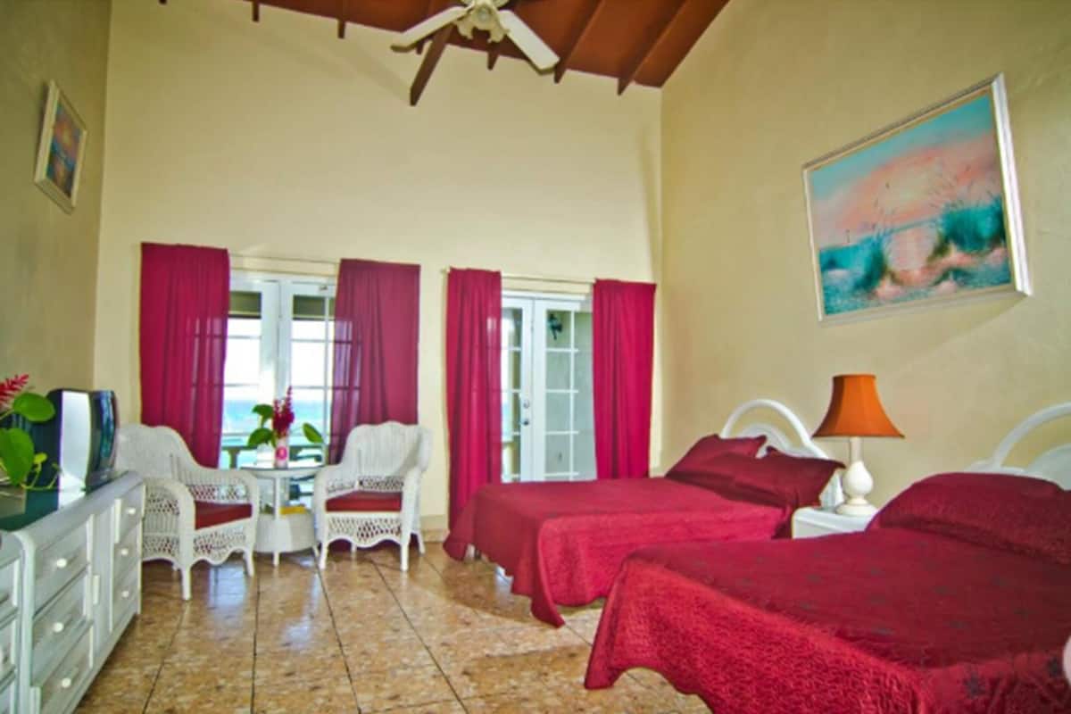 Quarto com duas camas, uma mesa de jantar com cadeiras, um ventilador de teto e um quadro na parede.
