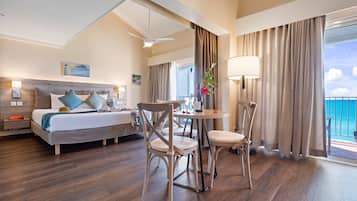 Quarto de hotel moderno com uma cama, uma mesa de jantar com cadeiras, varanda com cortinas e ventoinha no teto.