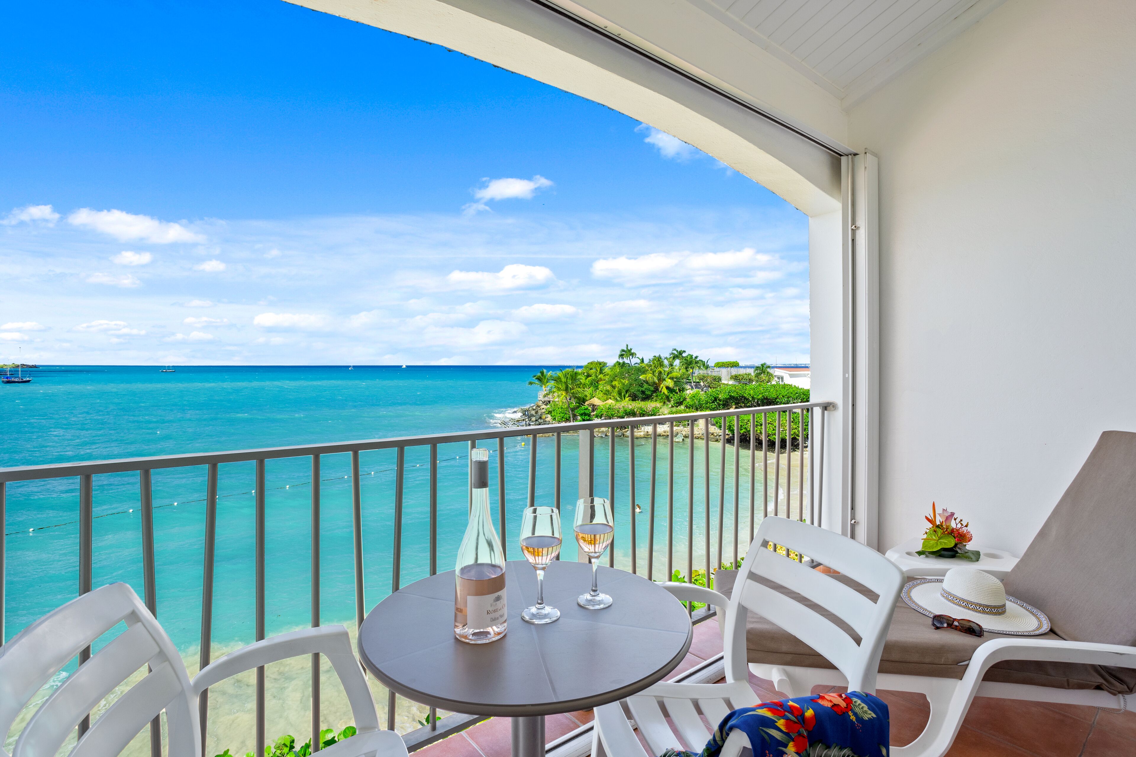 Varanda com mesa posta para dois, com vista para um mar azul-turquesa e a paisagem costeira.