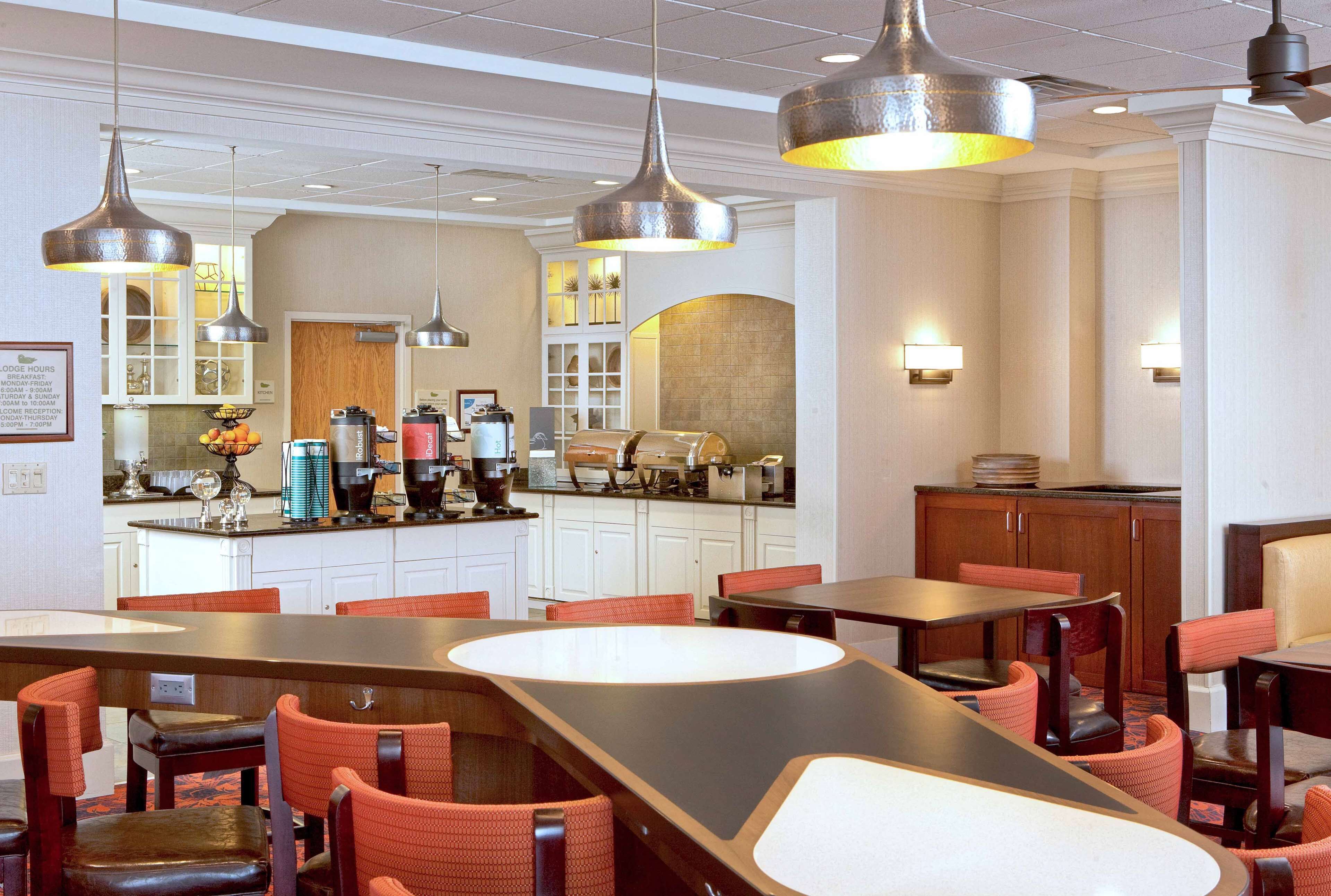 Um saguão de hotel com uma mesa de recepção, um canto para café e áreas de estar.