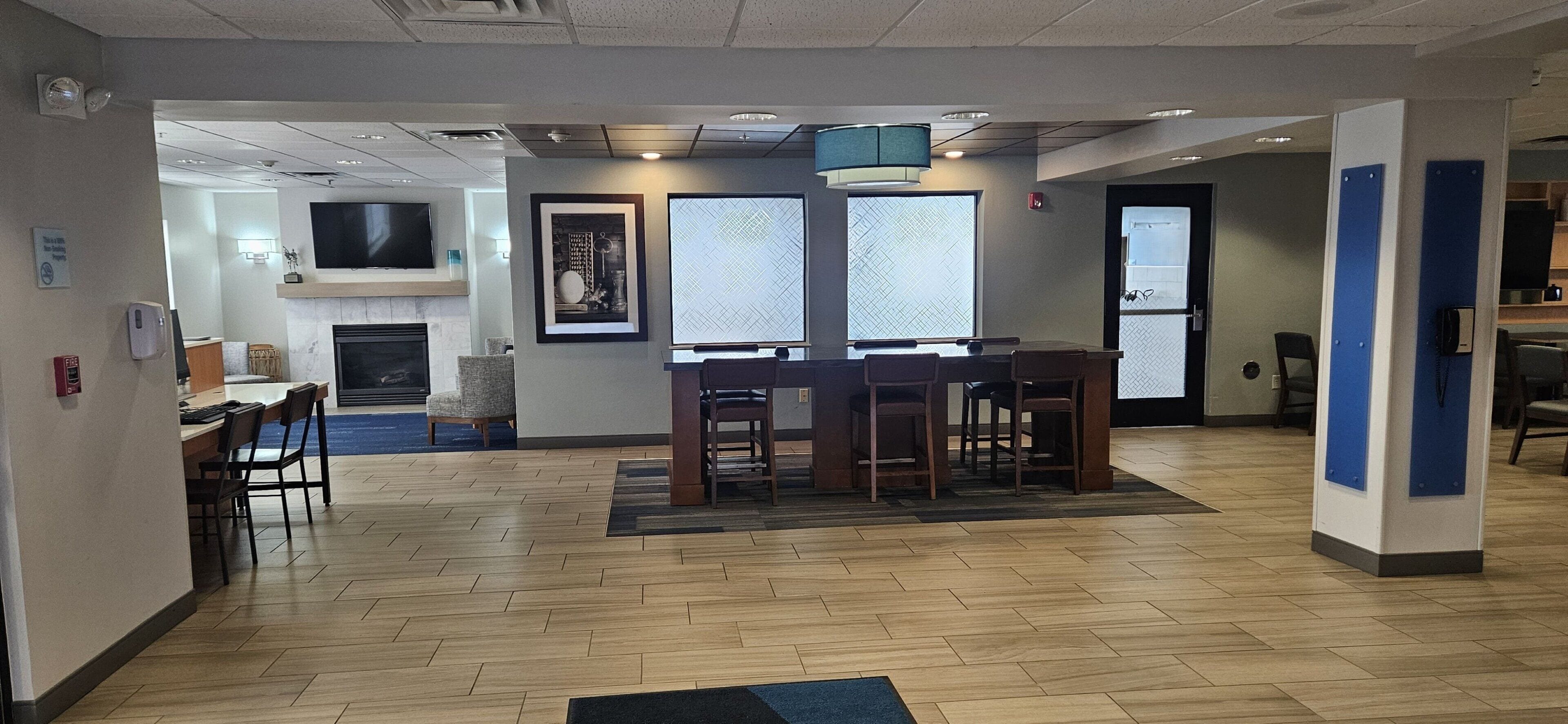 Um hall de hotel com lareira, televisão, obras de arte emolduradas e um espaço de refeições com cadeiras e mesa.