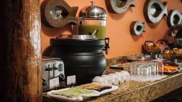 Disposição de buffet com uma cafeteira, uma panela grande e diversos alimentos sobre um balcão de granito.