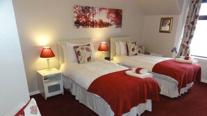 Quarto de hotel com duas camas, cada uma com um cobertor e almofadas vermelhos, roupa de cama branca e uma luminária vermelha em uma mesa de cabeceira.