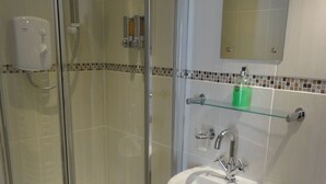 Um banheiro com chuveiro em box de vidro, pia branca e vaso sanitário.