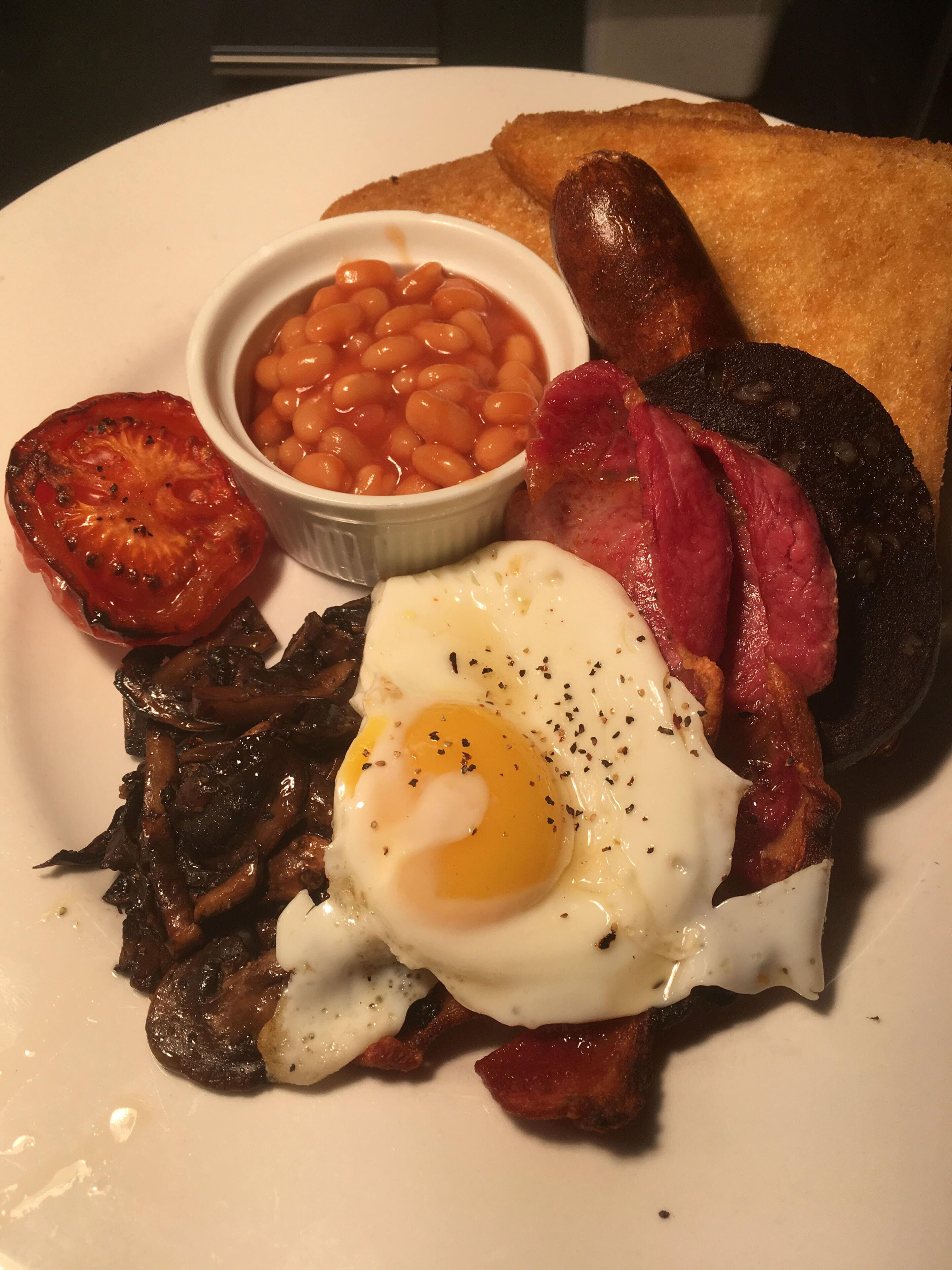 Um prato com ovo frito, bacon, salsichas, torradas, feijão e tomate grelhado.