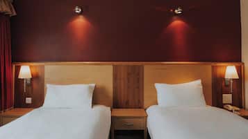 Quarto de hotel com duas camas, cabeceira de madeira, abajures e uma pequena gaveta.