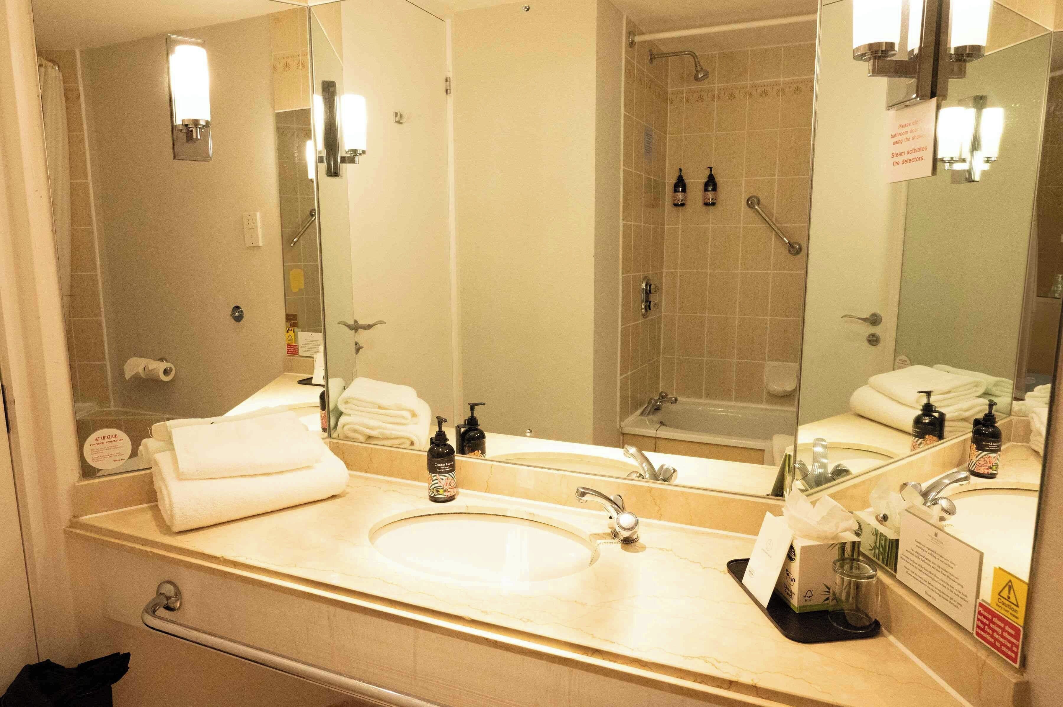 Casa de banho de hotel com um espelho grande, duas pias, chuveiro e porta-toalhas.