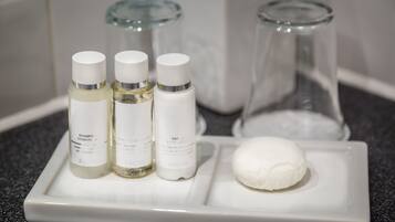 Uma bancada de banheiro com três frascos de shampoo e condicionador, uma garrafa de vidro e uma barra de sabão.