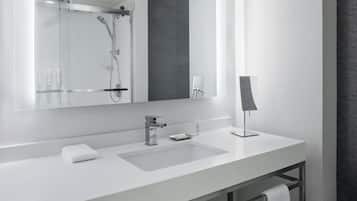 Uma casa de banho moderna com um espelho grande, chuveiro e lavatório branco.