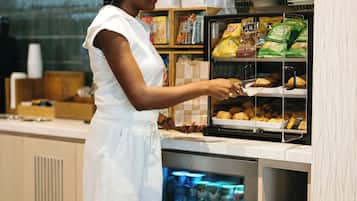Uma pessoa se servindo em um buffet com diversos alimentos e um refrigerador de bebidas.