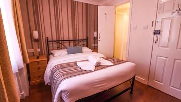 Cama bem arrumada com uma toalha enrolada, mesa de cabeceira com abajur, e porta com tranca.