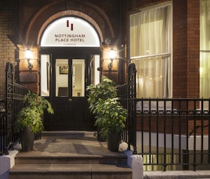 A entrada do Hotel Nottingham Place em Londres, com um portão de ferro preto, plantas em vasos e uma placa sobre a porta.