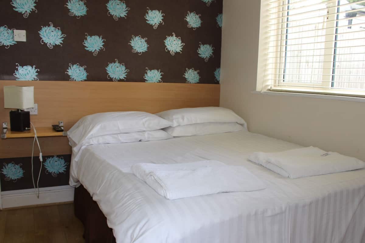 Uma cama bem arrumada com lençóis brancos, cabeceira de madeira e parede com padrão floral.