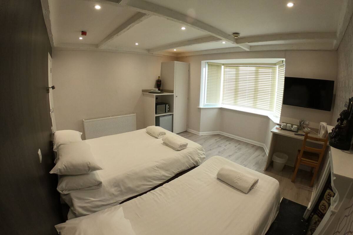 Quarto com duas camas, um radiador, uma TV e uma janela com persianas.