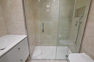 Uma casa de banho moderna com cabine de duche em vidro, uma sanita e uma pia branca.