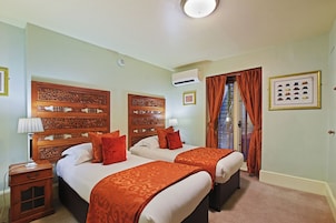 Quarto de hotel com duas camas, uma mesa de cabeceira, uma luminária, aparelho de ar condicionado e um quadro na parede.