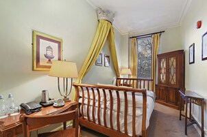 Quarto de hotel com cama, escrivaninha, telefone, luminária, armário e janela com cortinas.