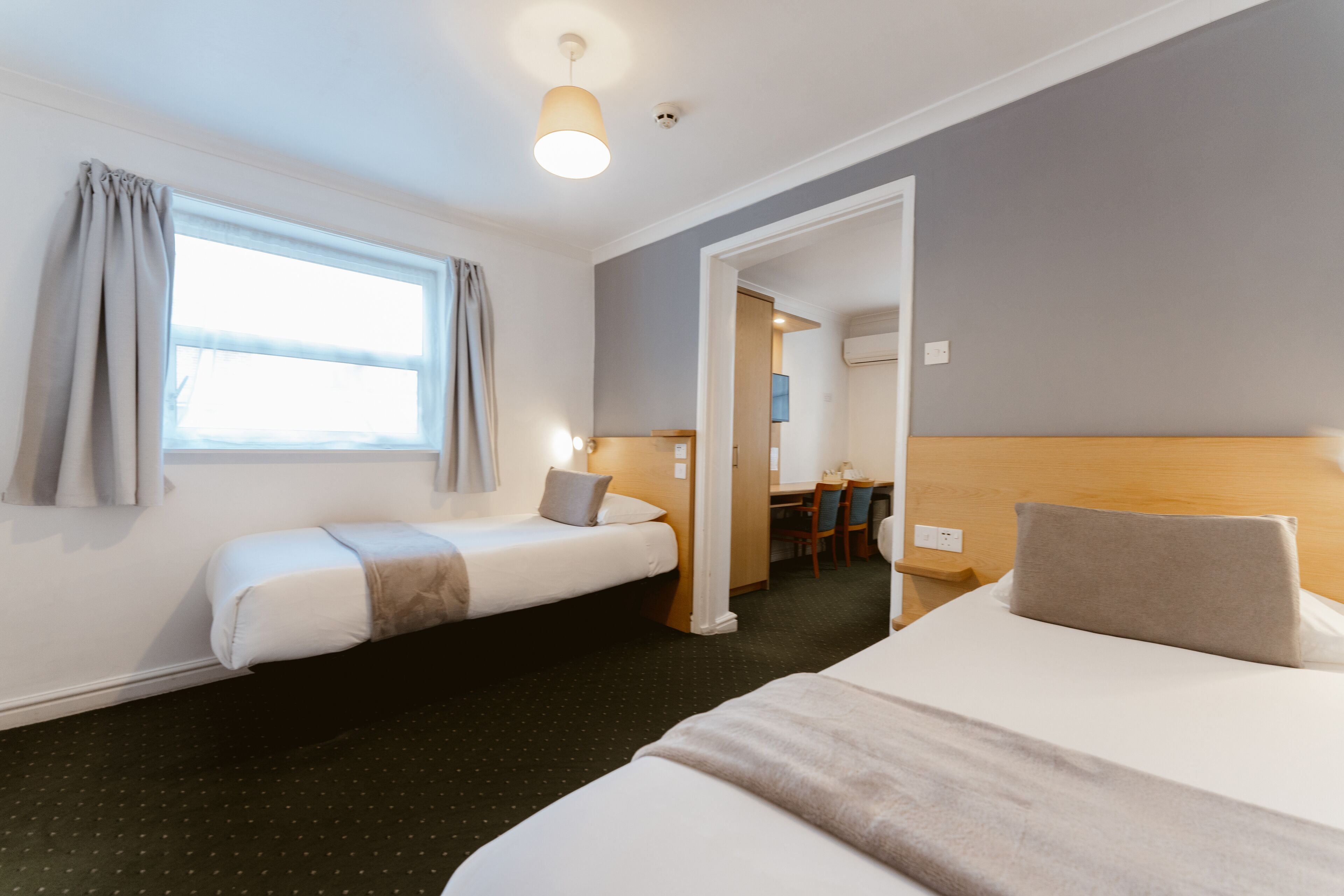 Quarto de hotel com duas camas de solteiro, uma escrivaninha e uma cadeira.