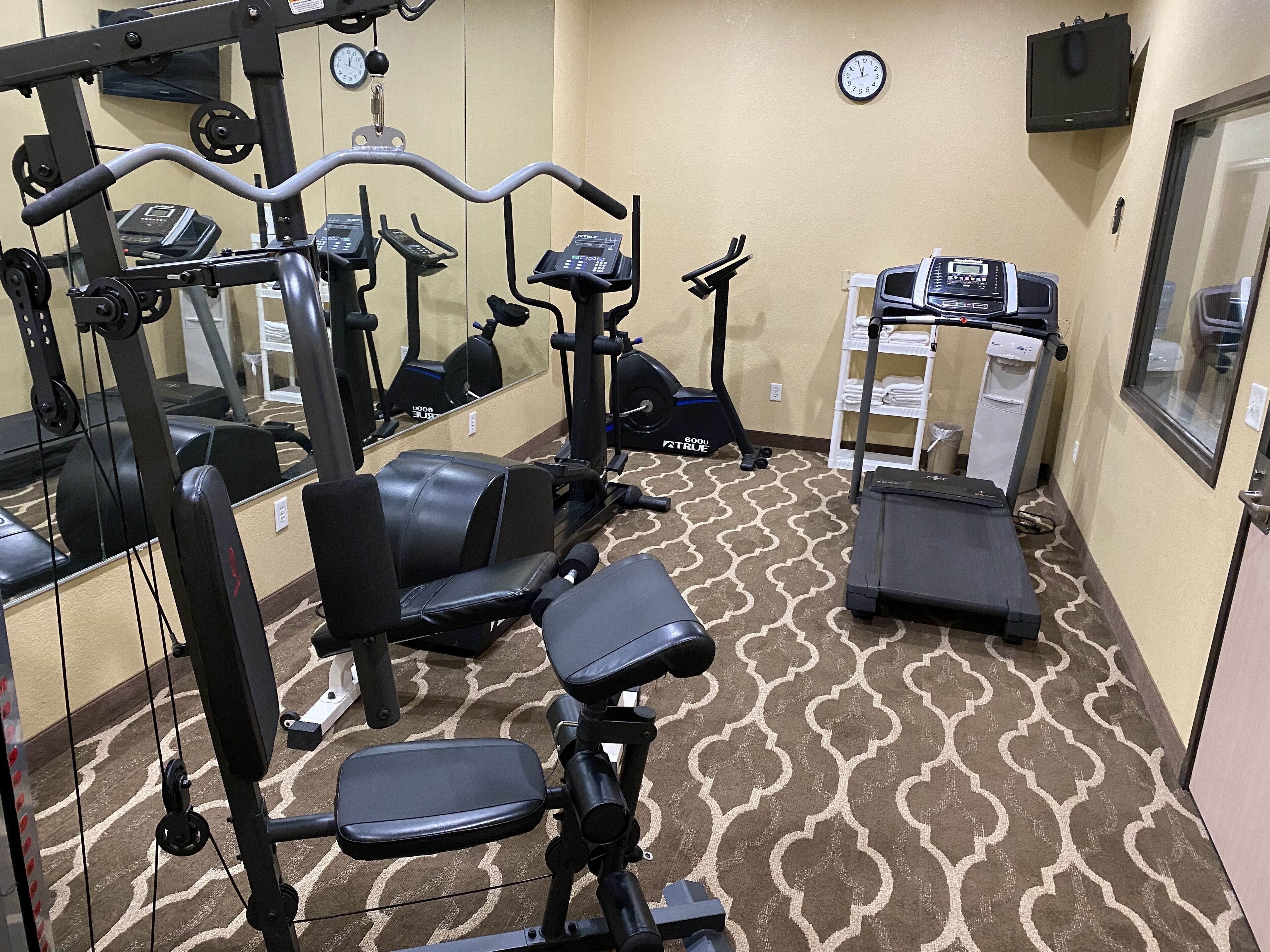 Uma academia com diversos equipamentos de exercícios, incluindo esteiras, máquinas de peso e uma barra para supino.