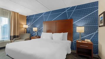 Quarto de hotel com uma cama grande, duas mesas de cabeceira com luminárias, uma cadeira e uma parede com padrão geométrico.