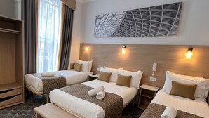 Quarto de hotel com duas camas, um banco, um guarda-roupa e uma grande obra de arte abstrata na parede.