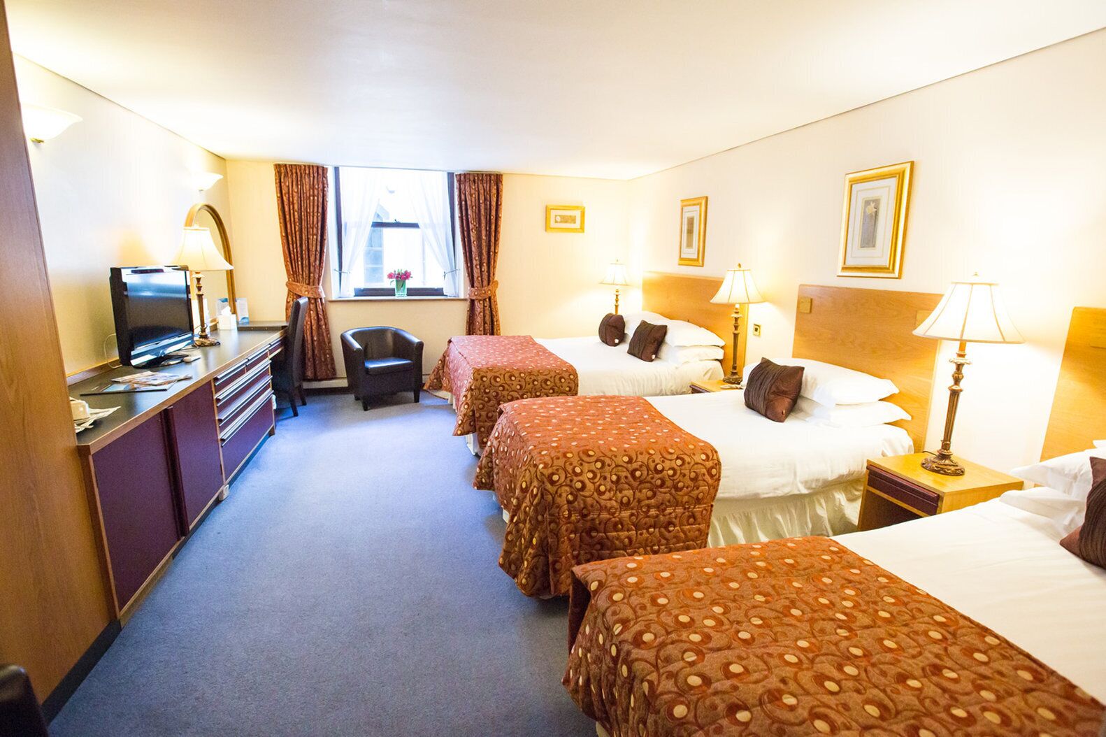 Quarto de hotel com três camas, uma secretária com televisão e uma cadeira.
