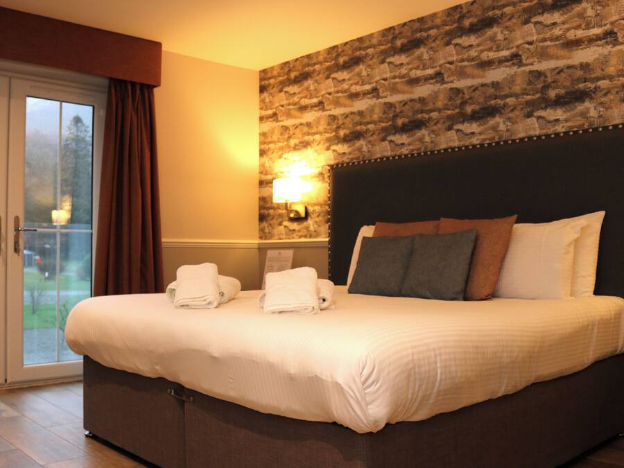 Quarto de hotel com uma cama grande, parede com padrão de tijolos e porta de vidro deslizante para uma varanda.