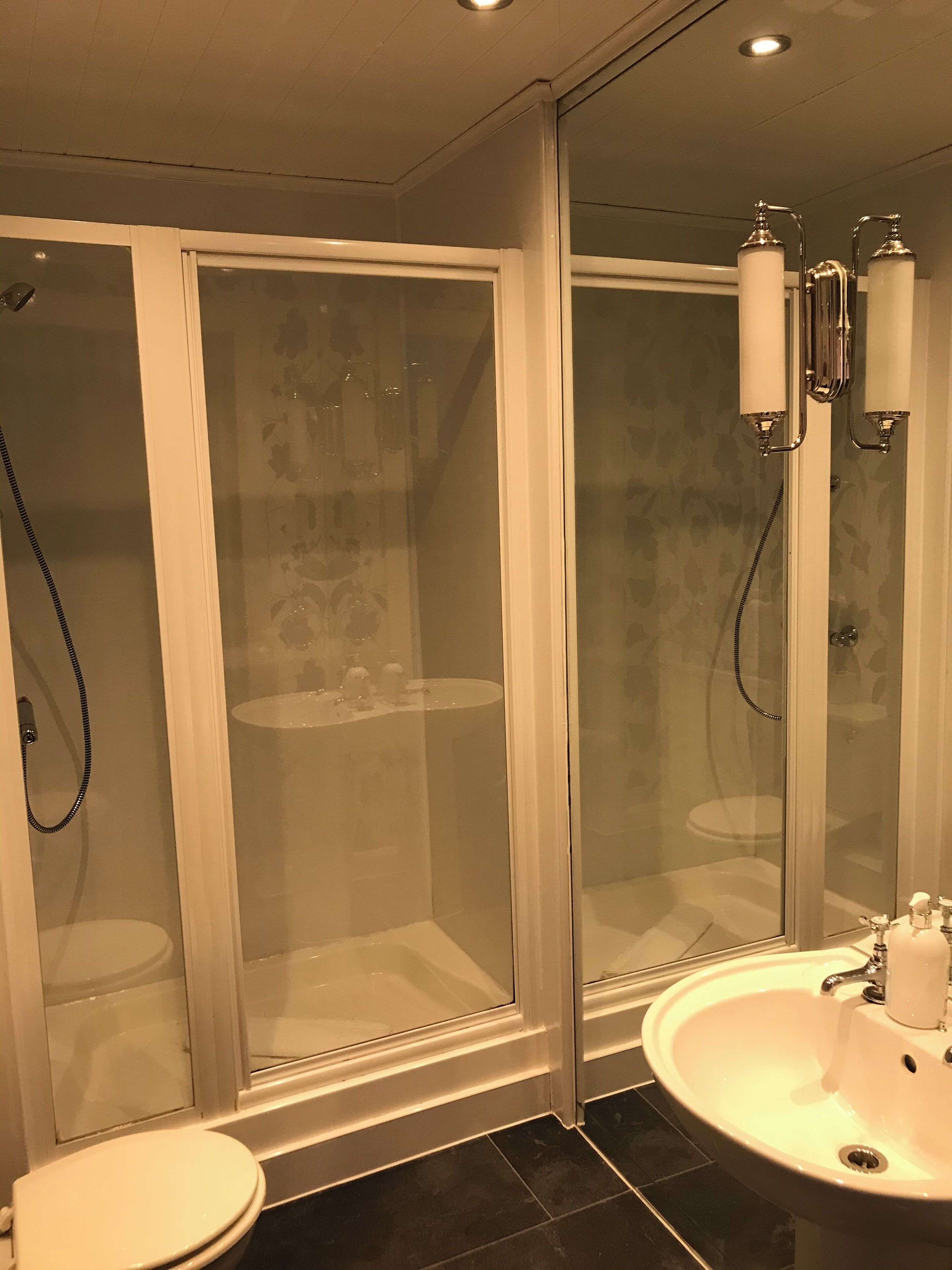 Um banheiro moderno com chuveiro em cabine de vidro, vaso sanitário branco e pia com espelho.