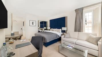 Quarto de hotel com cama, sofá, escrivaninha e mesa de centro de vidro.