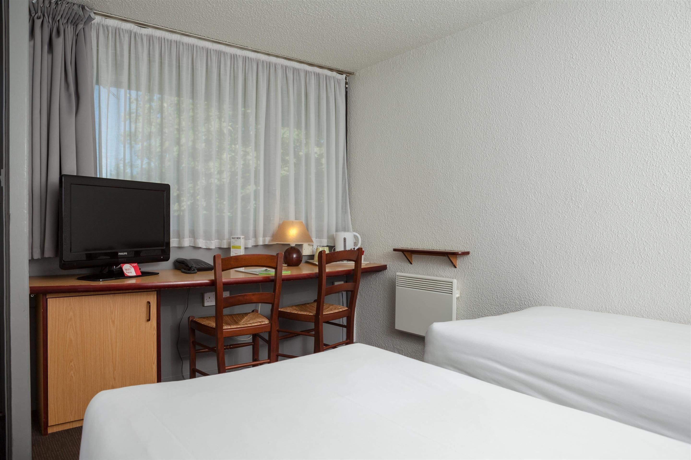 Quarto de hotel com cama, mesa de trabalho, televisão, cadeira e abajur.