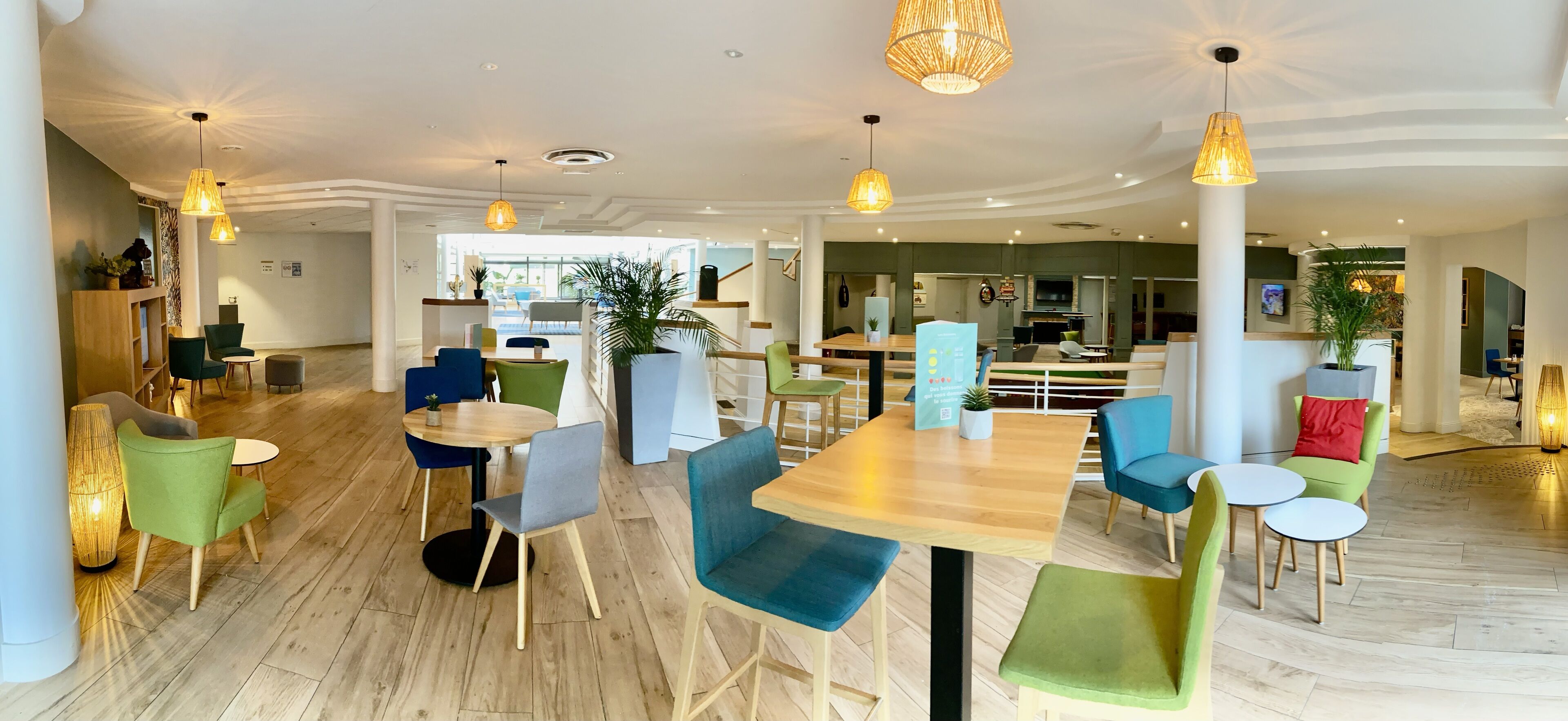 Um amplo hall de hotel com várias áreas de estar, incluindo mesas redondas e cadeiras, e uma área central com uma mesa comprida e cadeiras.