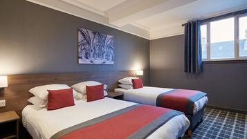Quarto de hotel com duas camas, uma mesa de cabeceira, uma obra de arte pendurada na parede, uma janela com cortinas e piso xadrez.