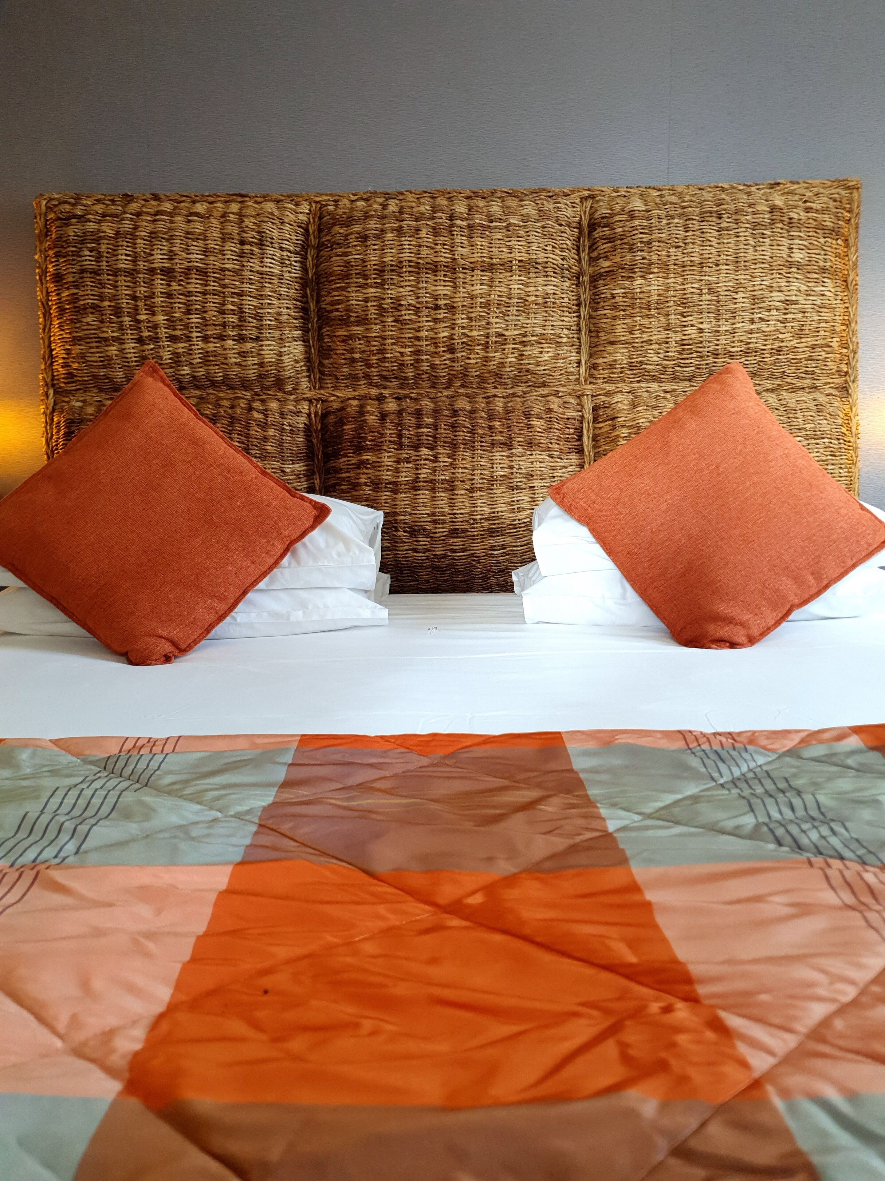 Cama com cabeceira de tecido trançado, duas almofadas e manta estampada.