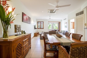 Uma ampla área de jantar com mesa e cadeiras de madeira, um vaso decorativo com plantas e um ventilador de teto.