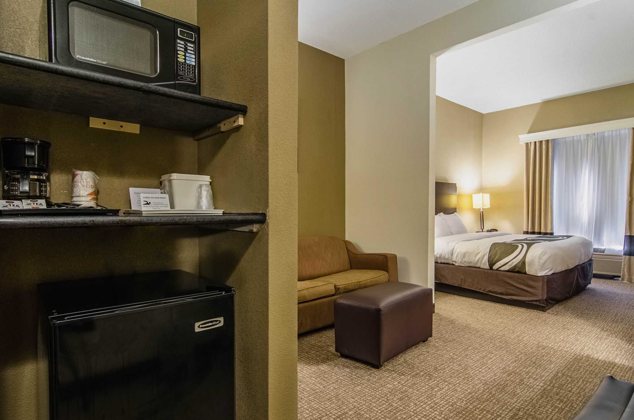 Quarto de hotel com cozinha compacta, cama, sofá e janela com cortinas.