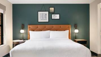 Quarto de hotel com uma cama grande, duas mesas de cabeceira, uma janela e obras de arte na parede.