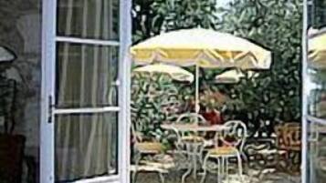 Um pátio aberto com mesa e cadeiras, um guarda-sol amarelo e vista para o verde lá fora.