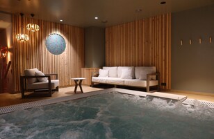 Um quarto de spa com hidromassagem, um sofá, uma poltrona e painéis de madeira.