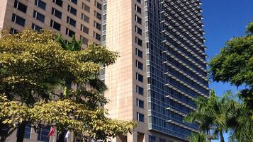 Um edifício alto com fachada de vidro moderna, cercado por palmeiras e uma área ajardinada bem cuidada.