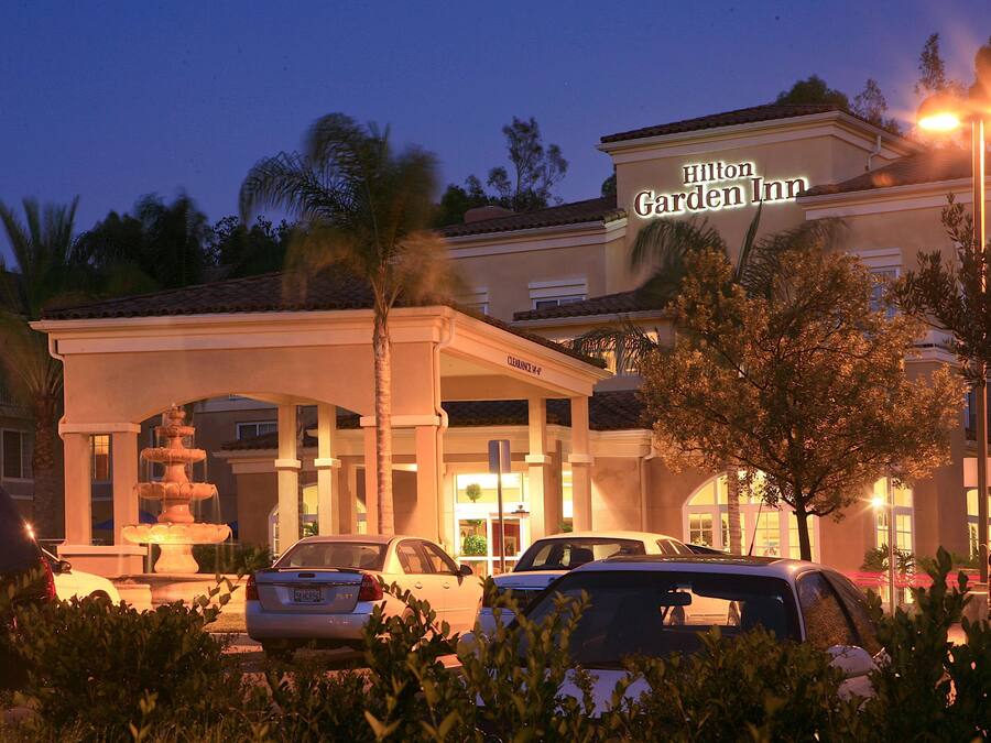 Um Hilton Garden Inn com uma fonte, carros estacionados e palmeiras.