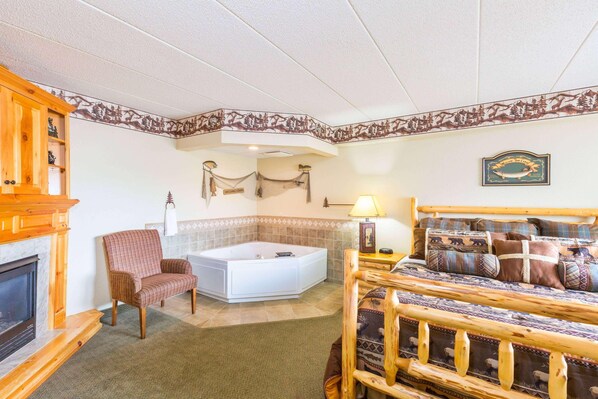 Quarto com lareira, uma banheira grande, cama com roupa de cama estampada e um armário de madeira.