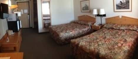 Quarto de hotel com duas camas, uma escrivaninha, uma cadeira, uma televisão e uma porta que dá para outro quarto.