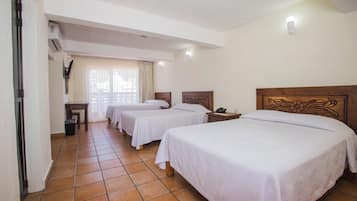 Quarto de hotel com três camas, uma mesinha e uma janela com cortinas.