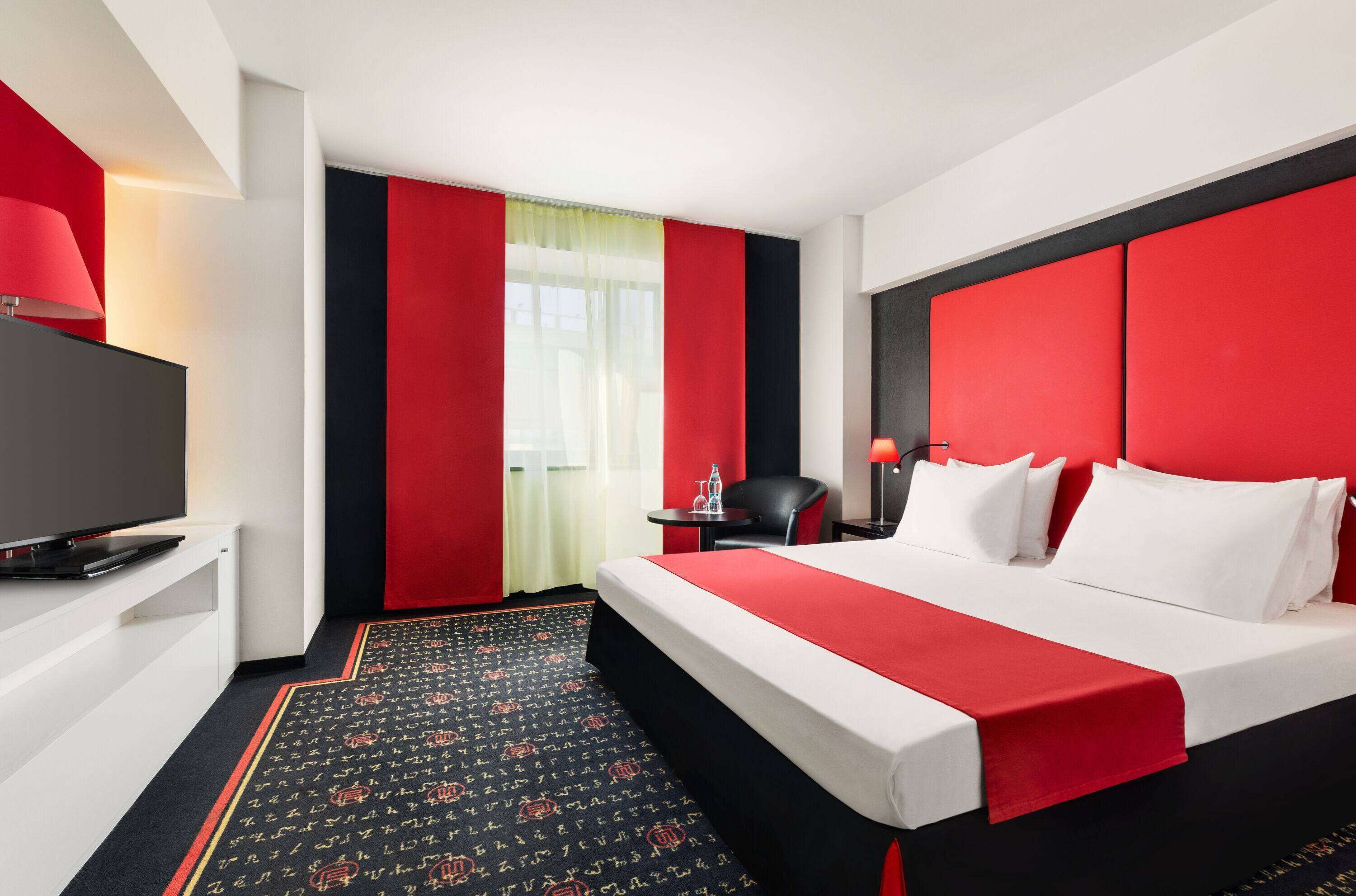 Quarto de hotel com uma cama grande, televisão, escrivaninha e uma cadeira.