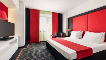 Quarto de hotel com uma cama grande, televisão, escrivaninha e uma cadeira.