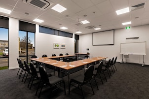 Sala de conferências com uma mesa comprida, cadeiras, tela de projetor e quadro branco.