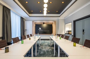 Uma sala de conferências com uma mesa comprida, cadeiras e uma tela exibindo o logotipo do Marriott Brussels Grand Place.