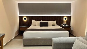 Quarto de hotel moderno com uma cama grande, mesas de cabeceira com abajures e um espaço de estar.
