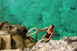 Uma pessoa sobe uma escadaria rochosa perto de um corpo d'água azul e límpido.